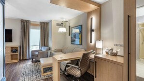 Quarto de hotel moderno com escrivaninha de madeira, poltrona estofada, sofá e televisão de tela plana.