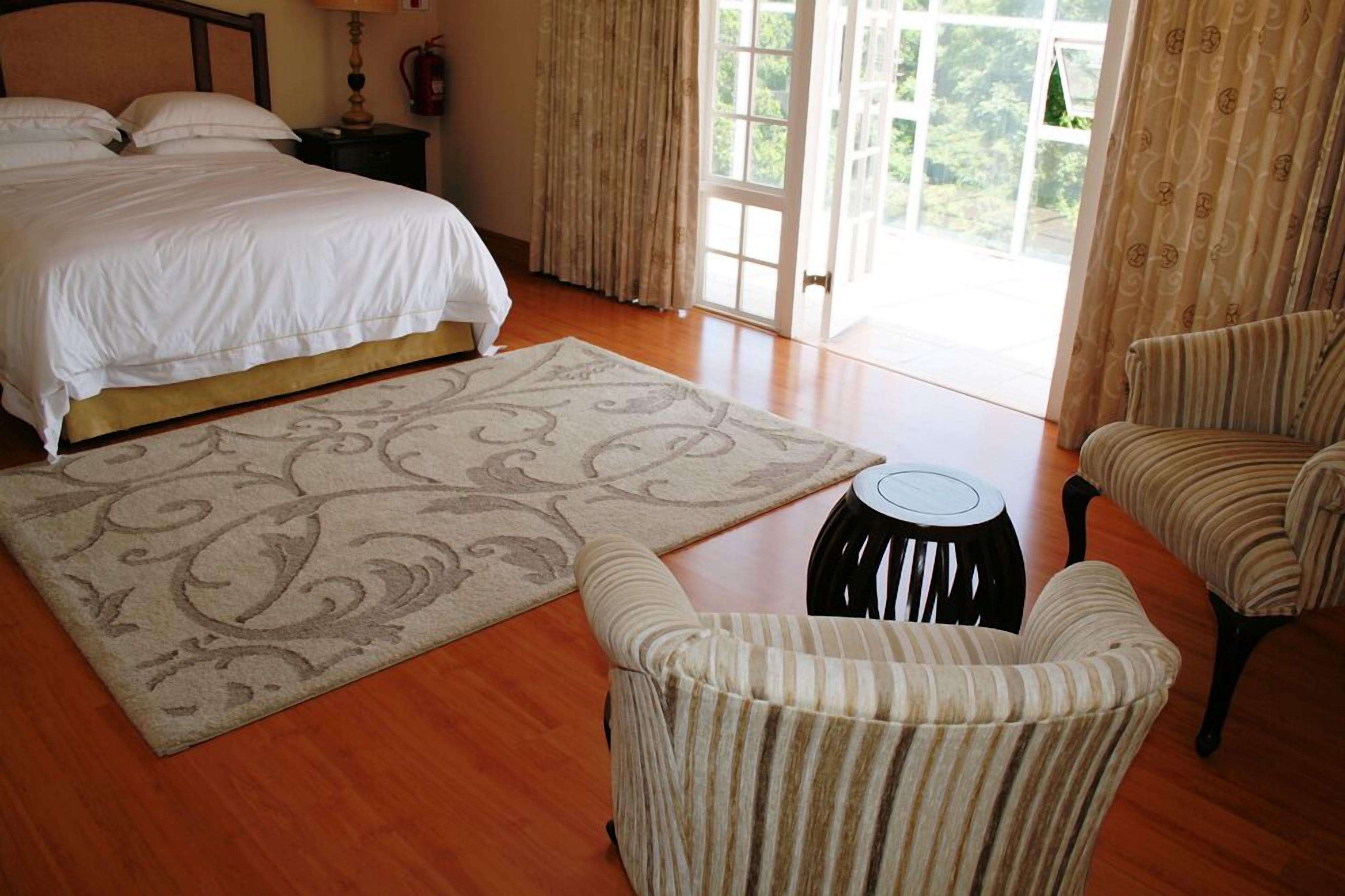 Quarto com cama, tapete estampado, cadeira e uma pequena mesa.