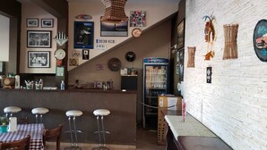 Interior de restaurante com área de bar, banquetas, geladeira e várias decorações nas paredes, incluindo relógios e quadros.