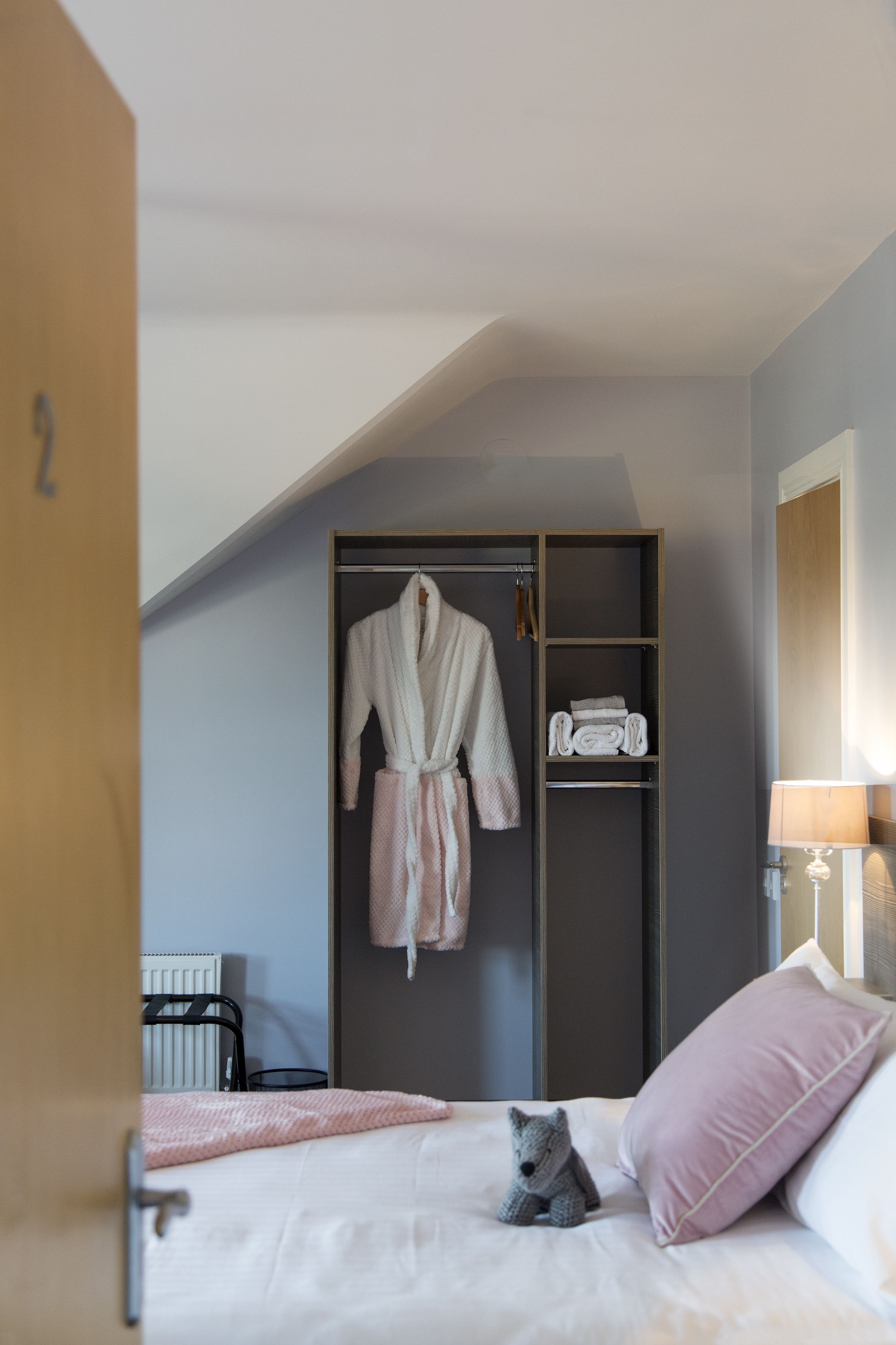 Quarto com cama, um urso de pelúcia, roupão e armário.