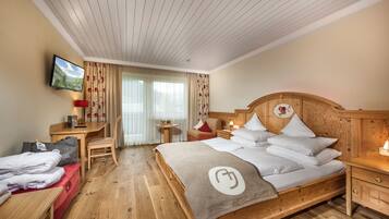 Quarto de hotel com uma cama de madeira, uma escrivaninha, uma cadeira, uma televisão e uma mesinha de cabeceira com abajur.