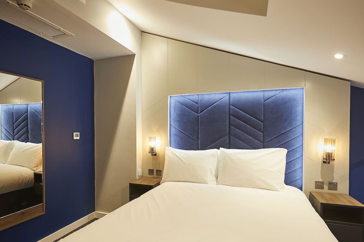 Quarto de hotel com uma cama grande, um espelho, duas mesas de cabeceira e um aplique de parede.
