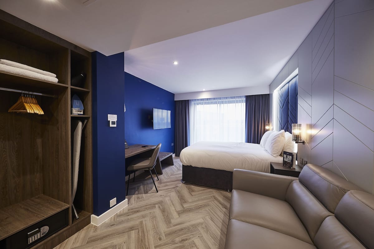 Quarto de hotel com cama, escrivaninha, cadeira, guarda-roupa e sofá.
