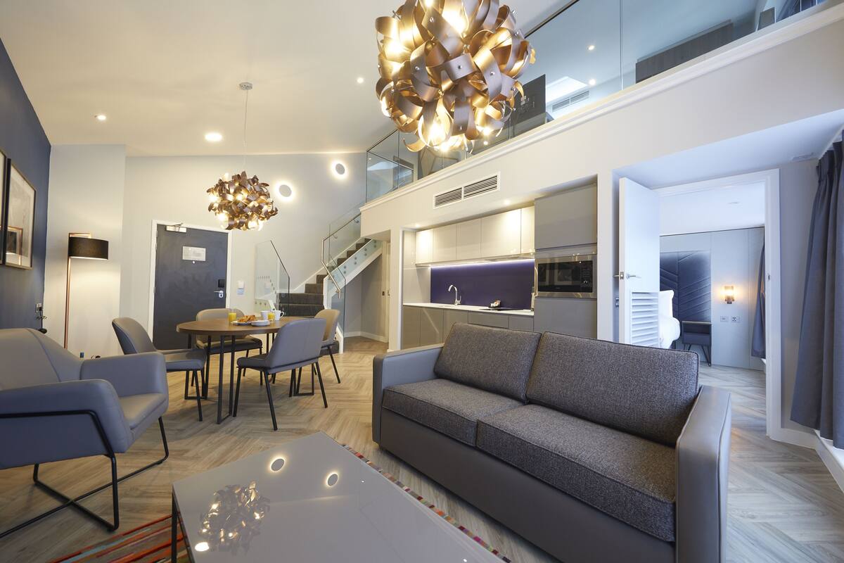 Uma sala de estar moderna com sofá, cadeiras, mesa de jantar e área de cozinha com escada.