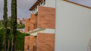 Um edifício moderno com piscina, rodeado por um jardim ajardinado e árvores altas.