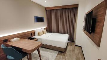 Quarto de hotel com cama, escrivaninha, cadeira, televisão e cortina.