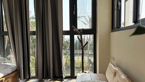 Quarto com um banco de madeira, uma cama com cabeceira e vista através de uma grande janela.