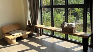 Quarto com uma janela ampla, um banco de madeira, uma mesinha e uma cesta de vime com toalhas.