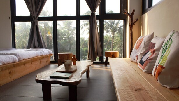 Quarto com cama de madeira, um banco de madeira, uma mesa pequena com um livro e um sofá com almofadas.