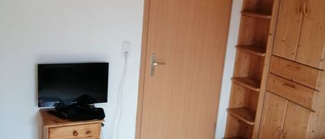 Quarto com guarda-roupa de madeira, televisão sobre um móvel de madeira e uma cadeira de madeira.