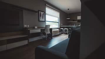 Uma sala de estar moderna com uma janela grande, uma escrivaninha, uma cadeira e uma área de cozinha com banquetas.