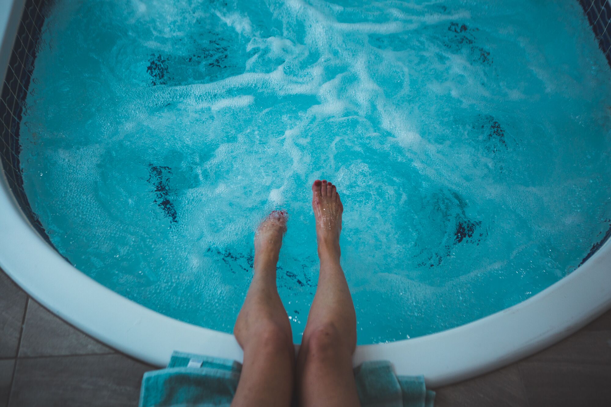 Uma pessoa relaxando em uma banheira de hidromassagem com bolhas visíveis e piso azulejado.
