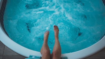 Uma pessoa relaxando em uma banheira de hidromassagem com bolhas visíveis e piso azulejado.