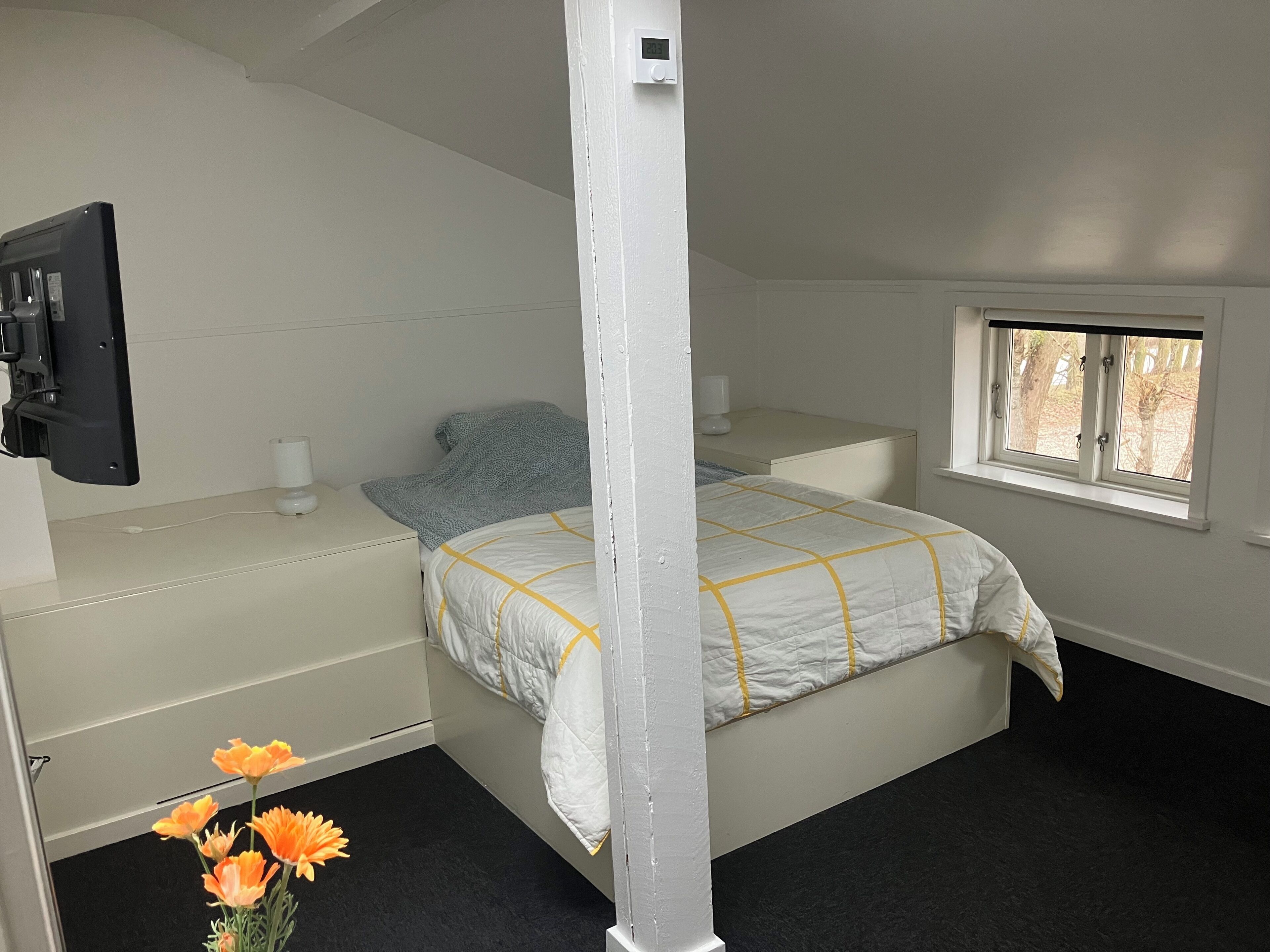 Quarto com cama, mesas de cabeceira, janela e televisão na parede.