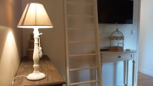 Um candeeiro branco sobre uma mesa de madeira, uma escada branca e um aparador branco com uma gaiola de pássaros.