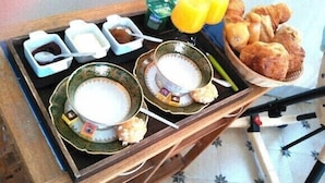 Uma bandeja de café da manhã com dois potes de cereal, uma garrafa de suco de laranja, uma cesta de croissants e pequenos recipientes com acompanhamentos.