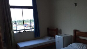 Quarto com duas camas, um pequeno frigorífico branco e uma janela com cortinas.