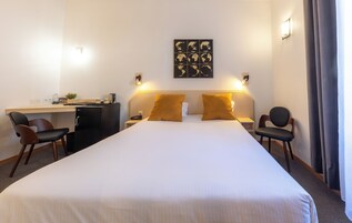Quarto de hotel com uma cama grande, duas cadeiras, uma escrivaninha e uma pintura de um mapa mundi na parede.
