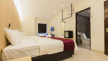Quarto de hotel moderno com cama, mesa de cabeceira, televisão e banheiro visível através de uma porta aberta.