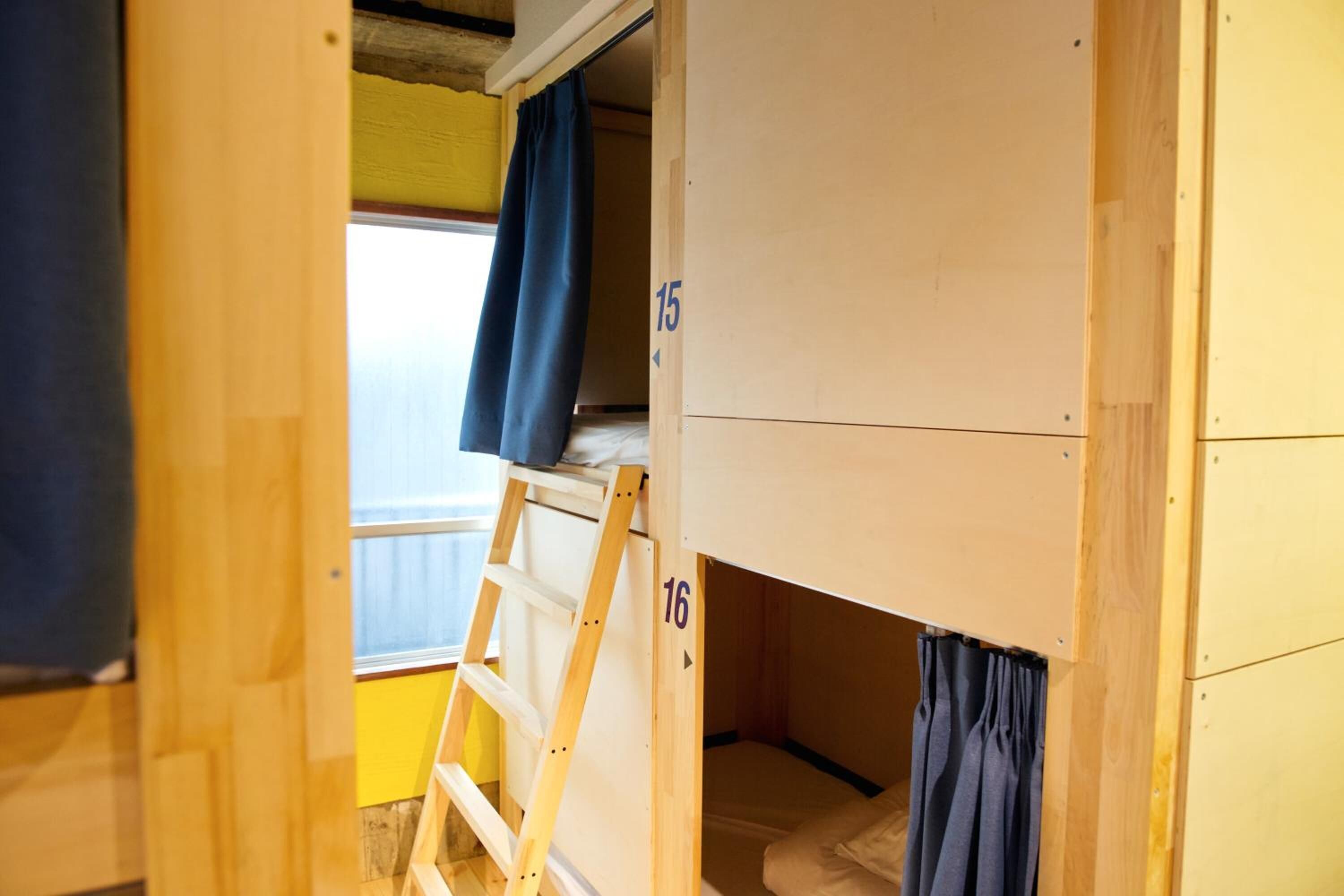 Quarto com beliche, escada, e os números 15 e 16 indicados nas camas, além de uma janela com cortinas.