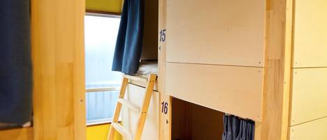 Quarto com beliche, escada, e os números 15 e 16 indicados nas camas, além de uma janela com cortinas.
