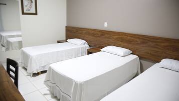 Quarto com três camas de solteiro, cabeceira de madeira, mesa branca e uma cadeira.