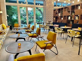 Uma área de estar moderna com mesas redondas, cadeiras amarelas e uma grande estante de livros.
