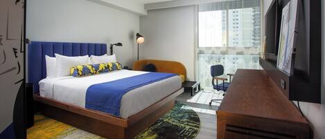 Quarto de hotel com cama, escrivaninha, cadeira, televisão e janela com vista para a cidade.