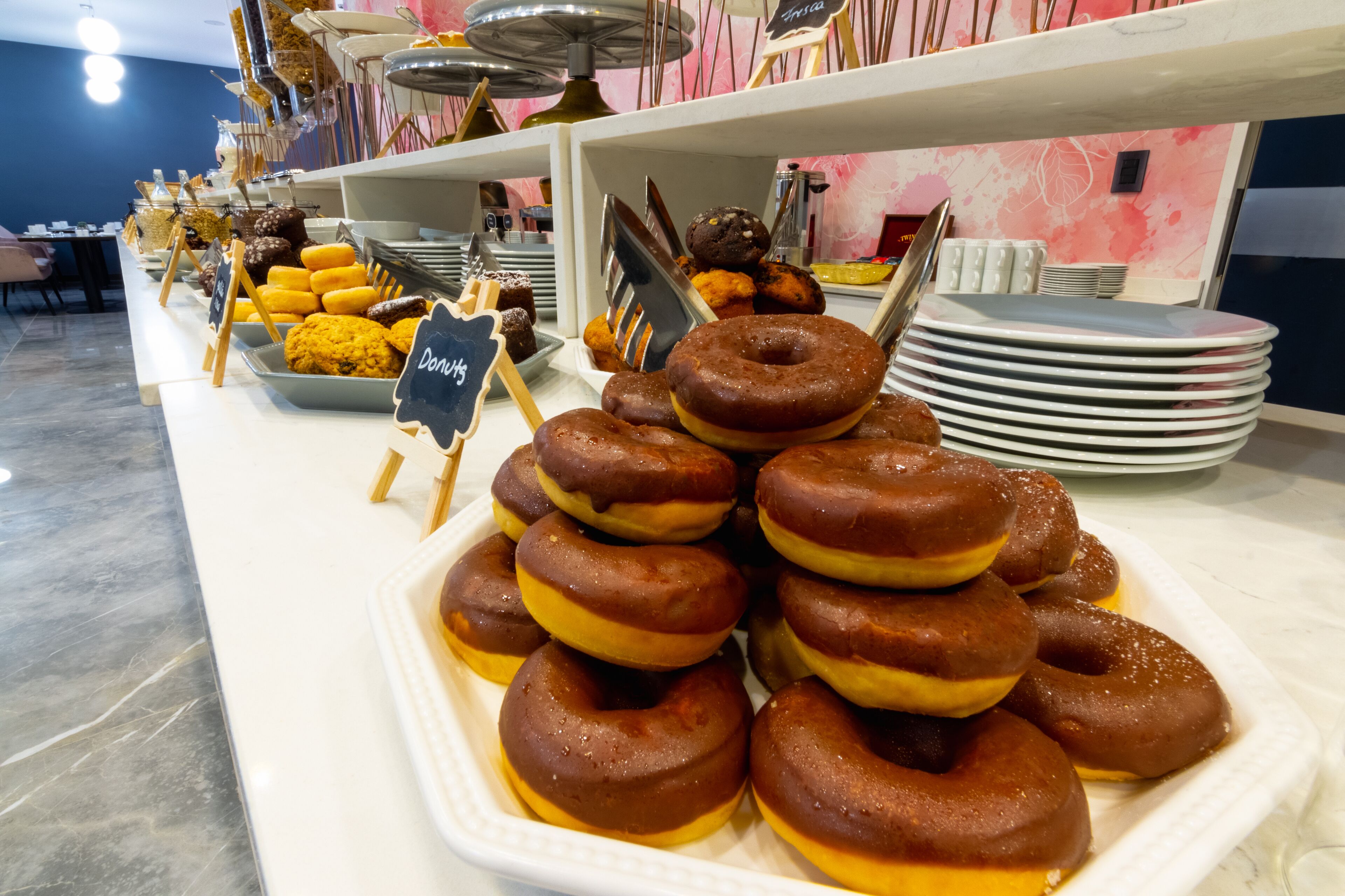 Buffet com diversos itens de comida, incluindo donuts, doces e um bolo de chocolate.