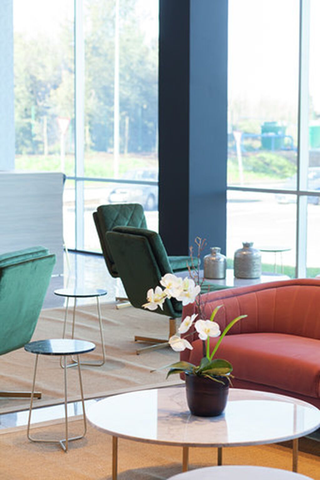 Um interior moderno com um sofá vermelho, poltrona verde e uma pequena mesa com uma orquídea em vaso.