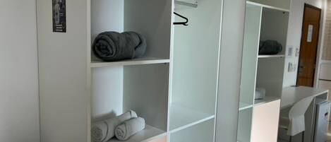 Quarto de hotel com um guarda-roupa branco, um espelho e uma escrivaninha.