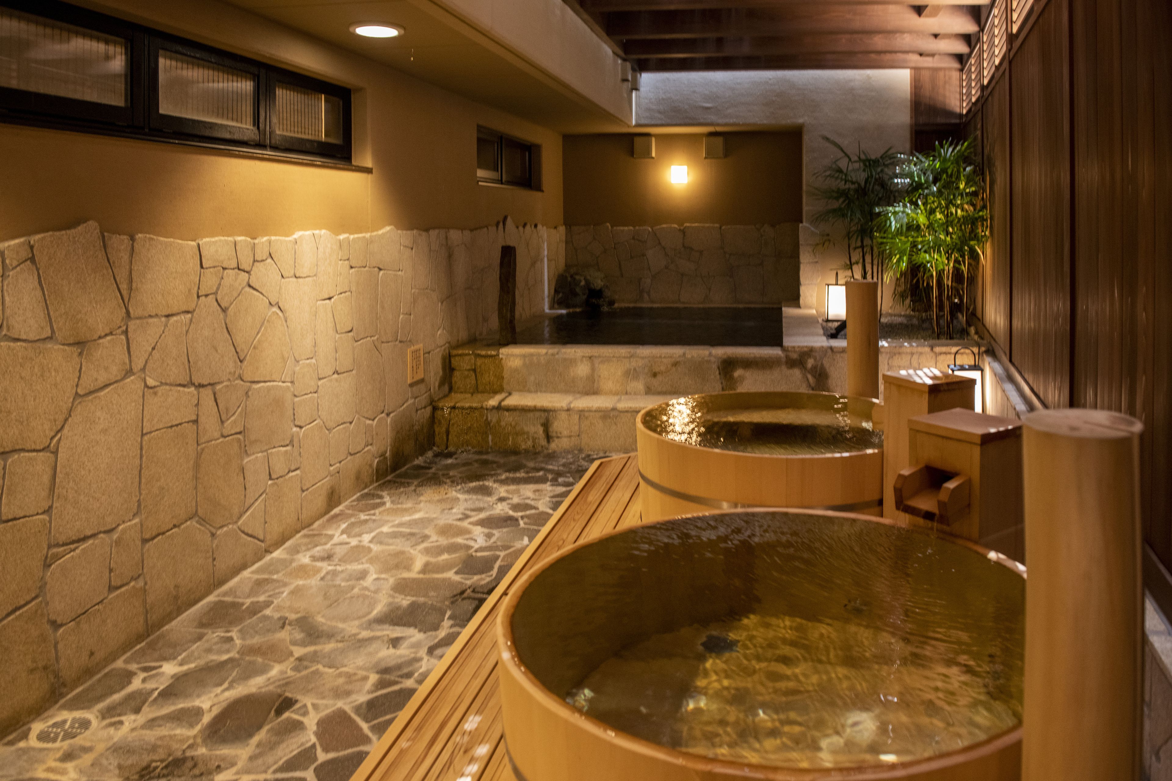 Uma área de spa com paredes de pedra, duas banheiras de hidromassagem e um banco de madeira.