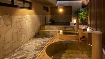Uma área de spa com paredes de pedra, duas banheiras de hidromassagem e um banco de madeira.