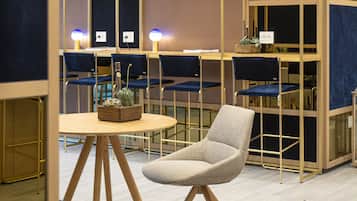 Um interior moderno com uma mesa de madeira redonda, uma cadeira estofada e uma estante com objetos decorativos.