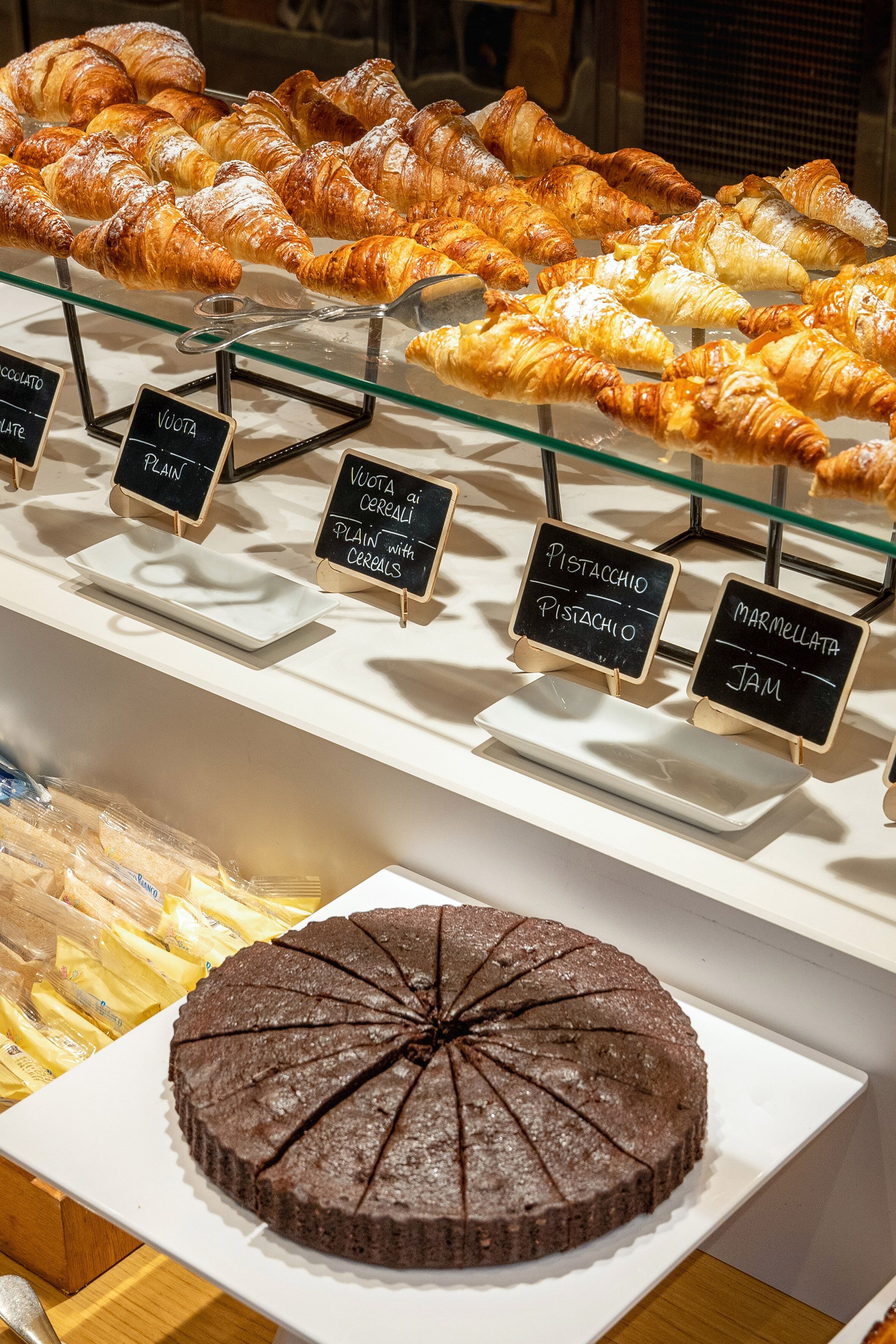 Vitrine de pastelaria com diversos doces e um bolo de chocolate.