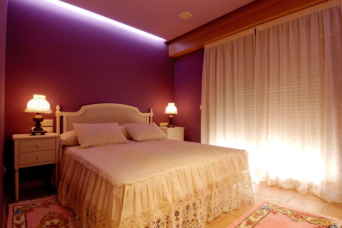 Quarto com uma cama, duas mesinhas de cabeceira e uma janela com cortinas.