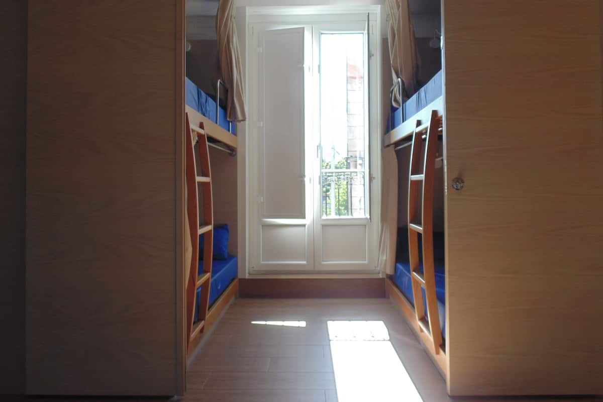 Quarto pequeno com duas camas beliche, uma porta e uma janela.
