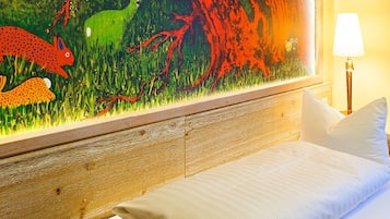 Quarto de hotel com uma cama, cortina listrada colorida, mural na parede com diversos peixes e uma luminária de cabeceira.