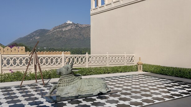 Um pátio com piso xadrez, uma estátua e uma montanha ao fundo.