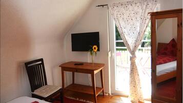 Quarto com uma cama, secretária de madeira, cadeira, televisão e janela com cortinas.