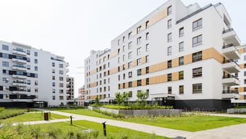 Um edifício moderno de apartamentos, com vários andares, varandas e um jardim bem cuidado, com caminhos e vegetação.