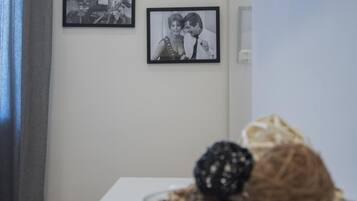 Quarto com uma mesa branca, duas fotografias preto e branco emolduradas na parede, e uma janela com vista para o exterior.