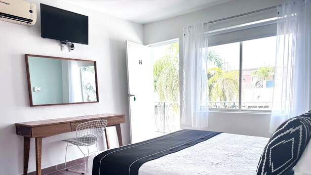 Quarto de hotel com cama, escrivaninha, cadeira, televisão e janela com cortinas.