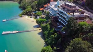 Vista aérea de uma área costeira com praia, um píer e um edifício de vários andares com sacadas.