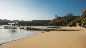 Uma praia com um iate atracado em um cais, rodeada por árvores e águas calmas.