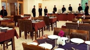 Uma sala de banquetes com várias mesas preparadas para refeições, teto de madeira e vista para o exterior.