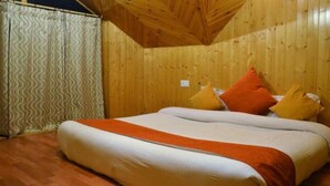 Quarto com teto de madeira, cama com roupa de cama branca e detalhes em laranja, e cortina estampada.