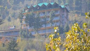 Um hotel com vários andares e telhado verde, rodeado de árvores.