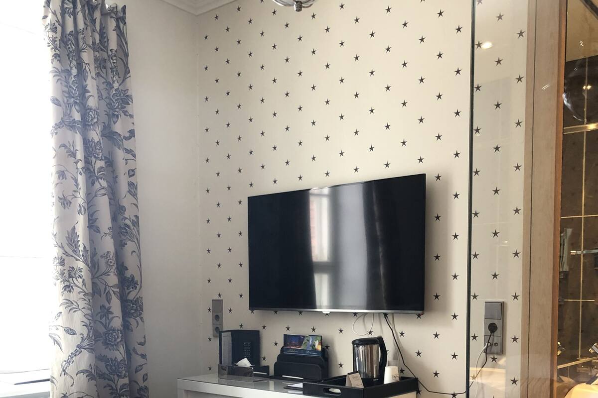 Quarto de hotel com cama, escrivaninha, televisão de tela plana, cafeteira e chuveiro.