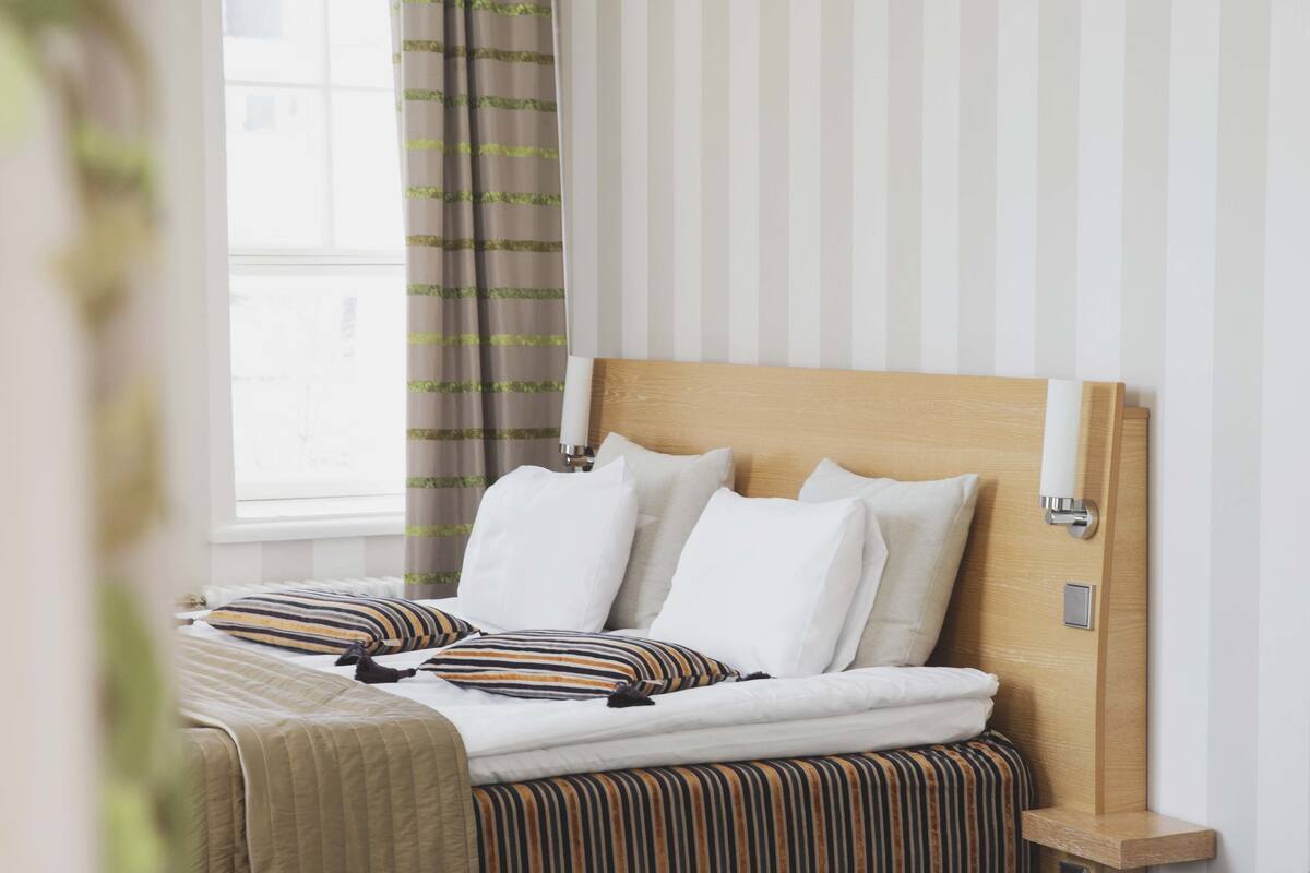 Quarto de hotel com cama, cortinas listradas e janela.